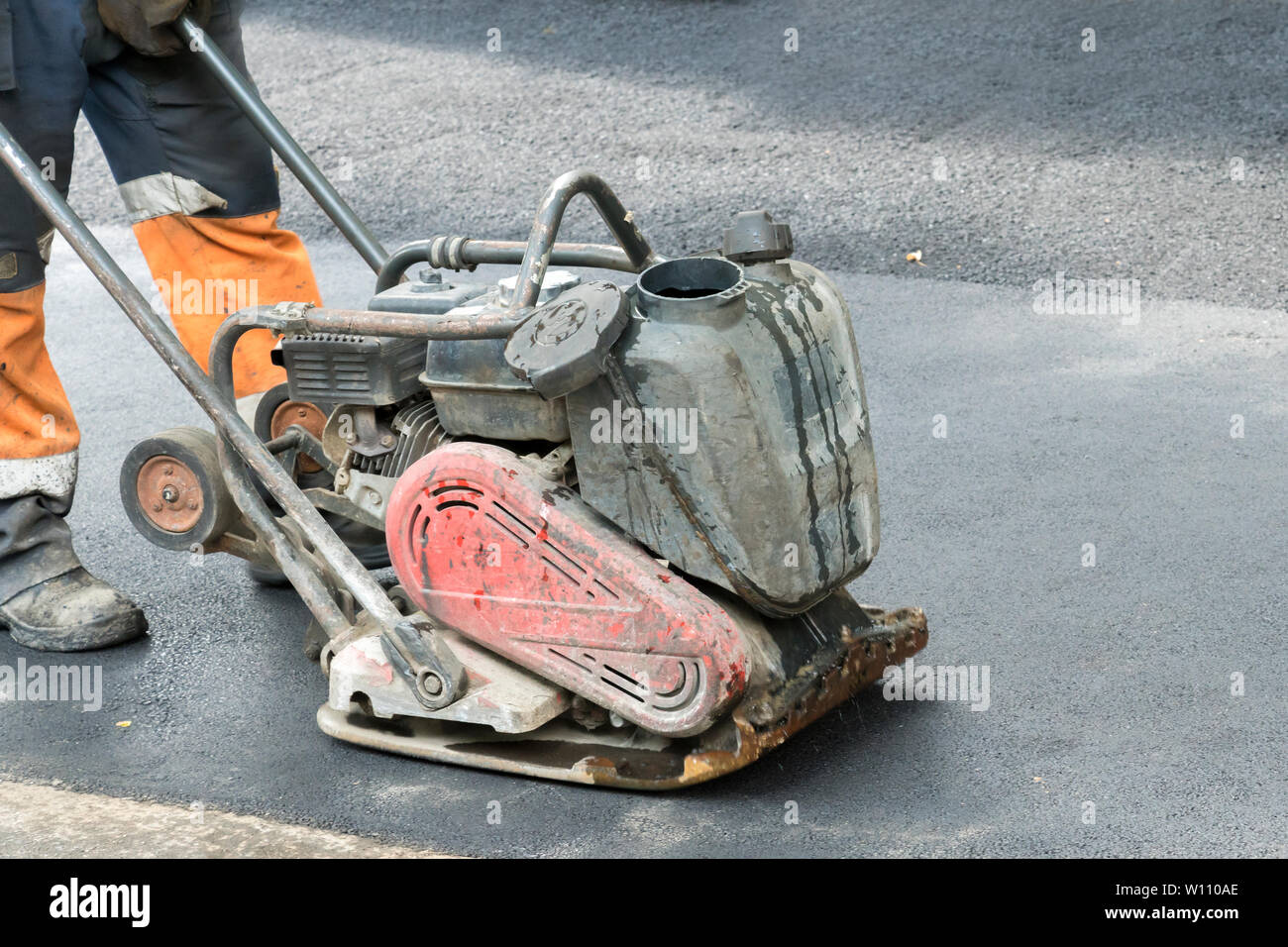 Road workers compact the asphalt with a vibrating rammer on the road ...