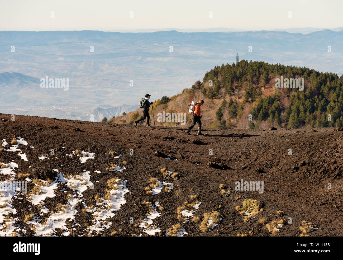 A couple of hikers walk along an extinct crater on the mount Etna ...