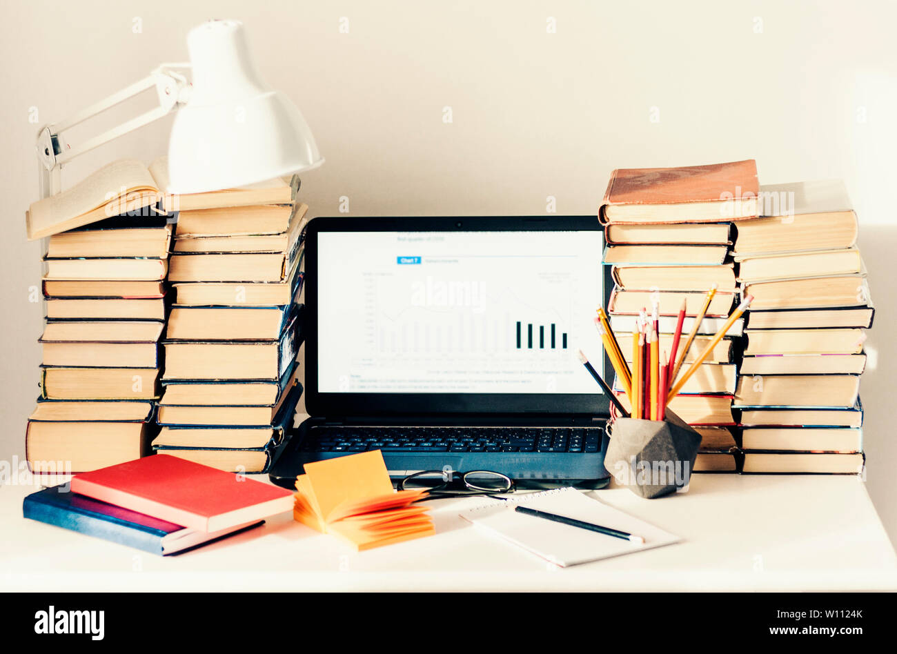 Laptop, stack of books, notebook, pencils in office background for ...