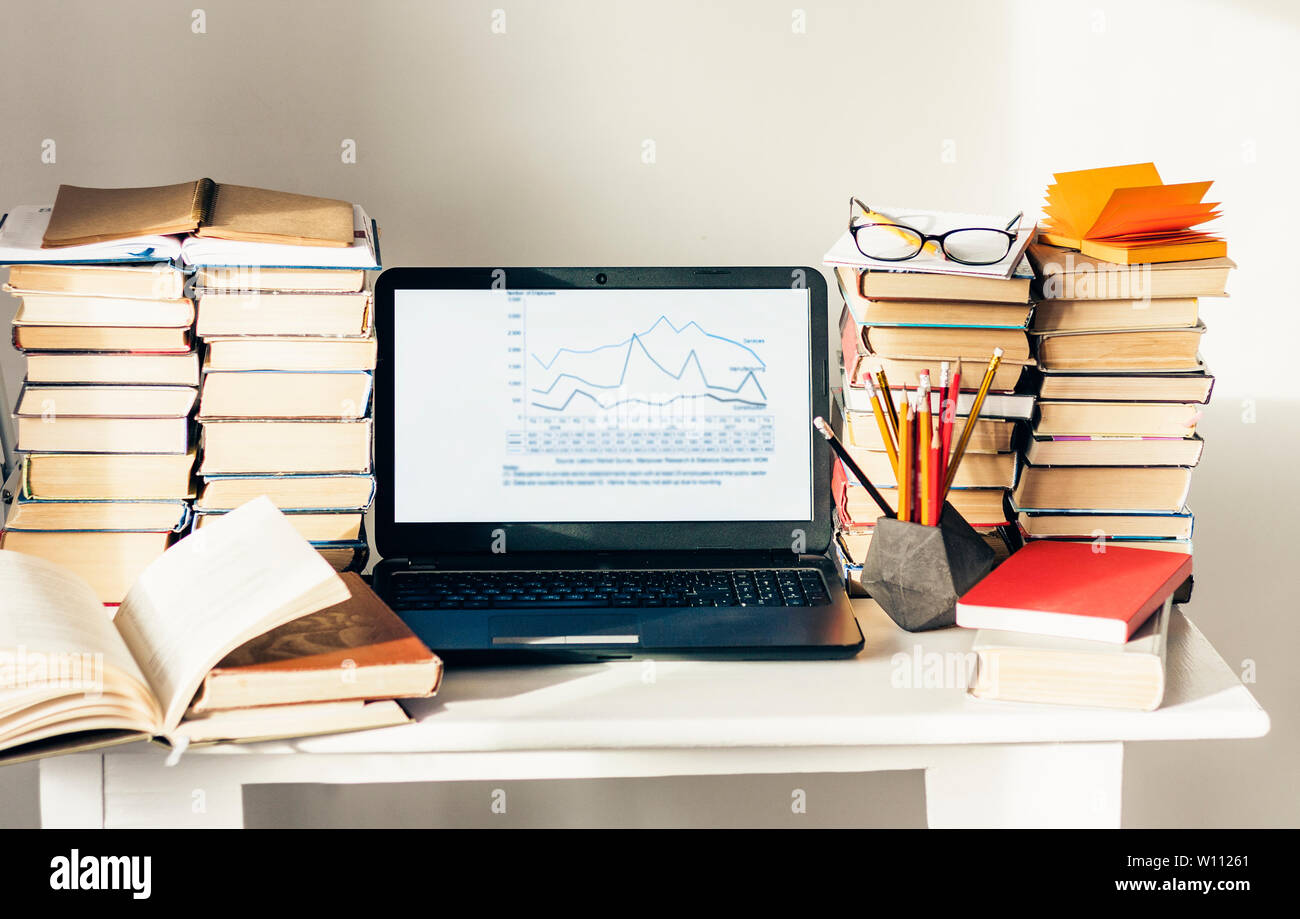 Laptop, stack of books, notebook, pencils in office background for ...
