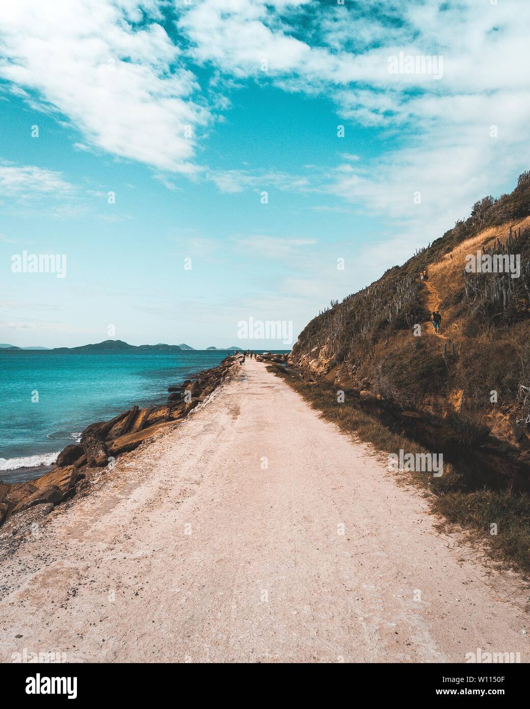 Narrow sandy road going alongside the sea and high steep hills with a ...