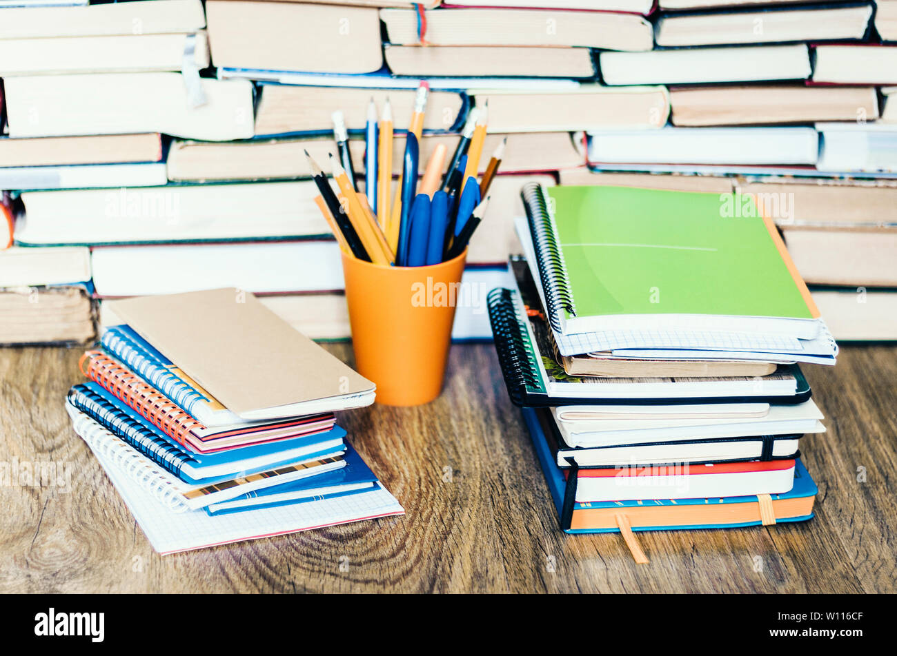 Stack of books, notebooks and pencils in plastic holder on wooden table ...
