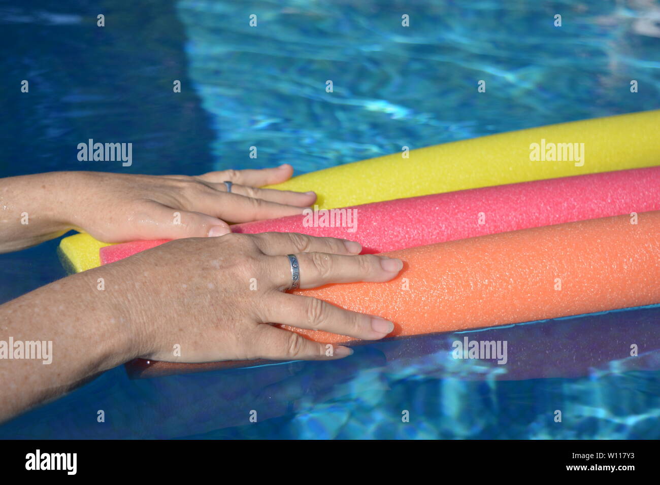 Woman's hand holding three brightly coloured pool noodles in a swimming ...