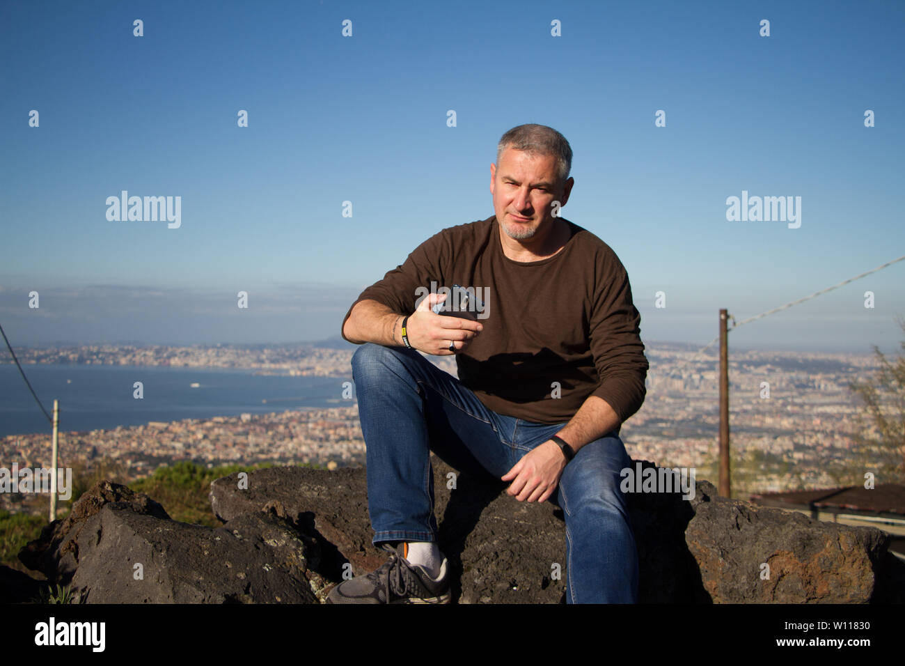 Adult gray-haired man with a beard sits on top of Mount Vesuvius with a ...