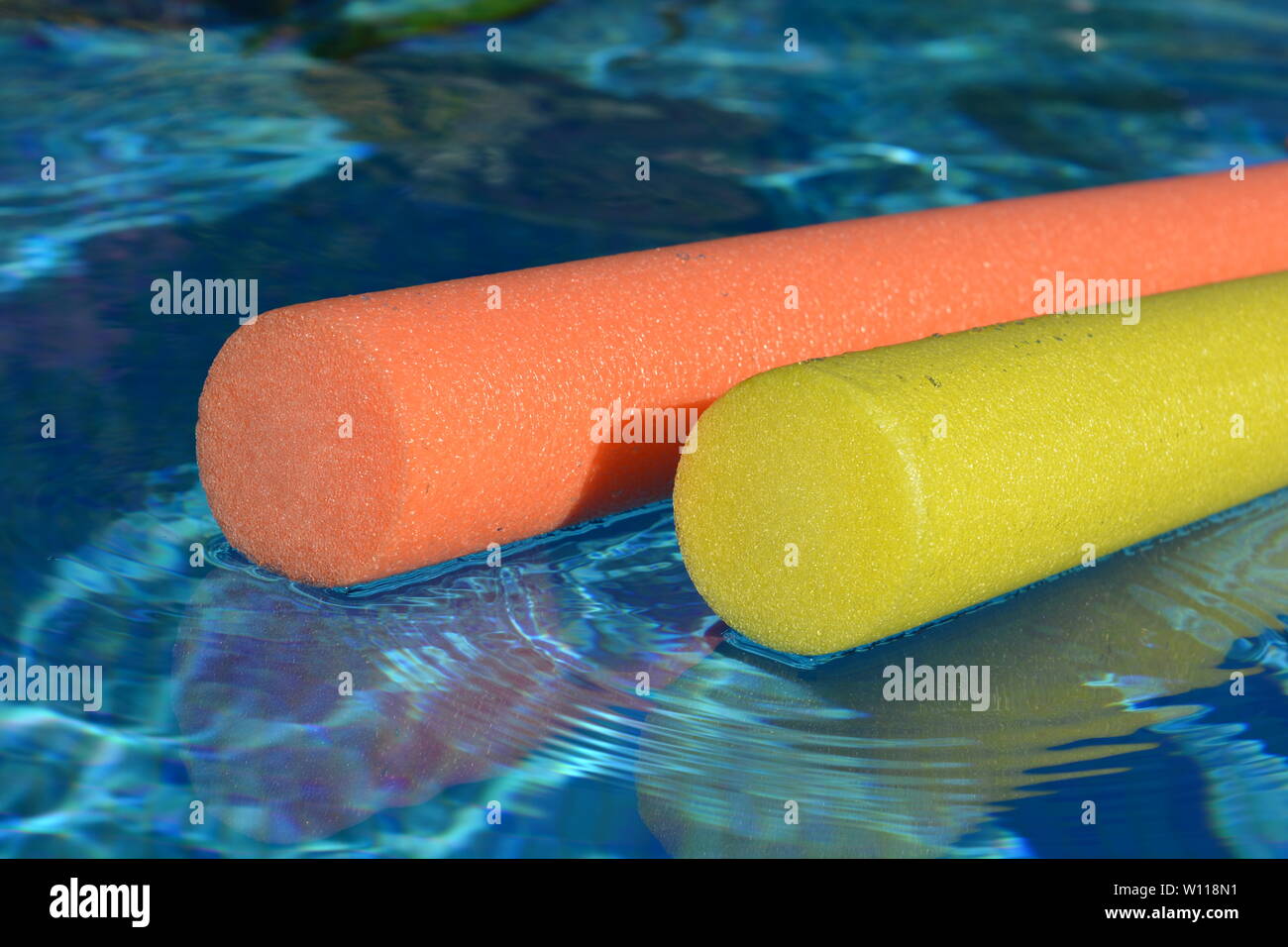 Brightly coloured pool noodles and swimming pool, with copy space. Fun ...