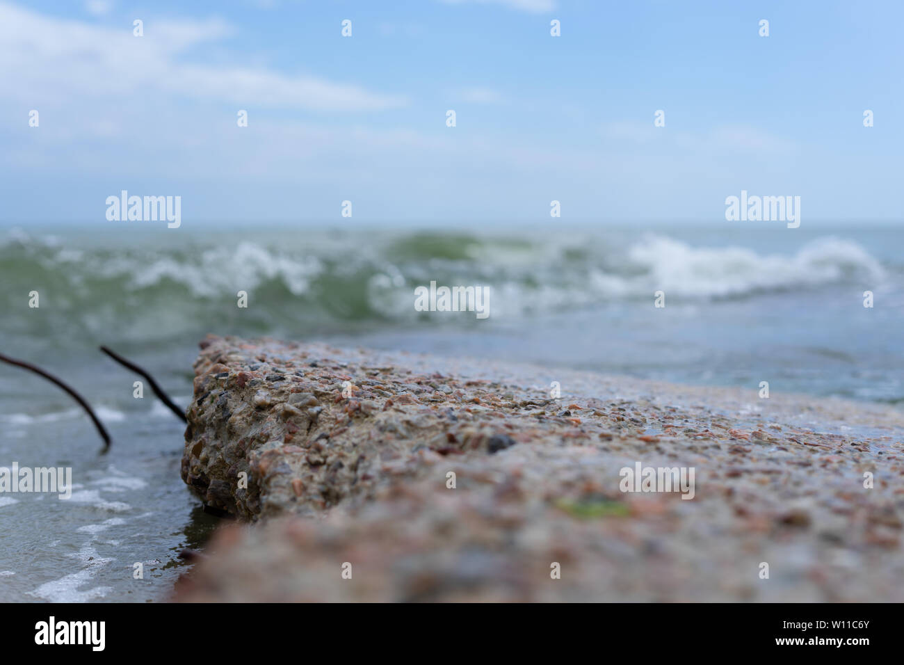 Concrete slab with protruding rusty reinforcement on the beach. Waves ...