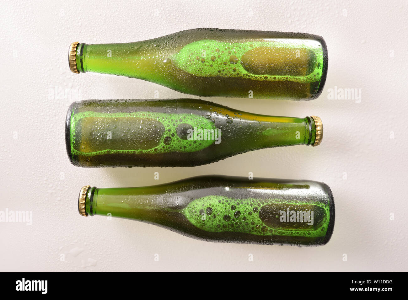 Three green bottles with alcoholic beverage on white table. Horizontal ...