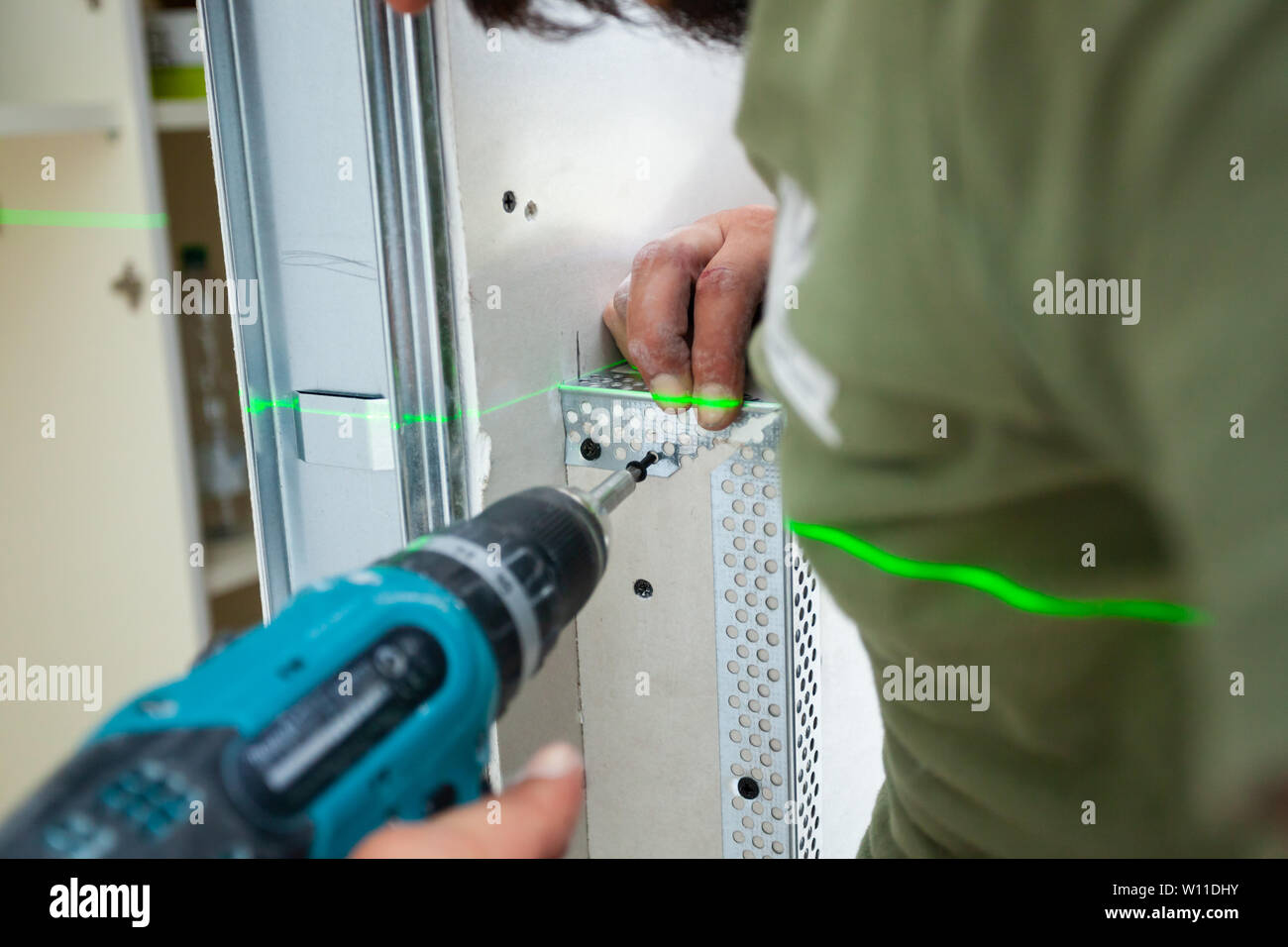 Worker building plasterboard wall. Working with cutting tools, fixing ...
