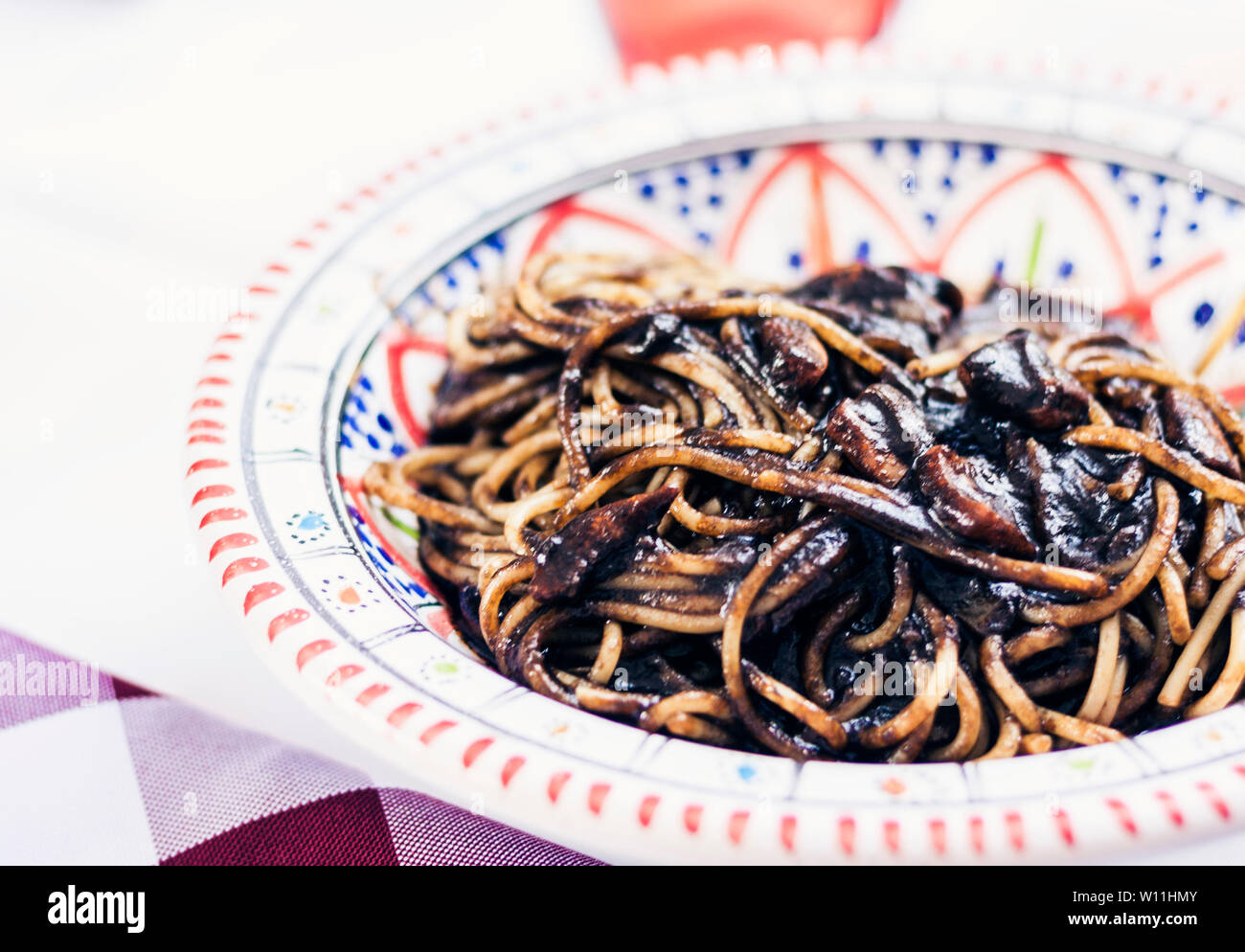 Black squid ink pasta on the plate with red-blue pattern in the ...