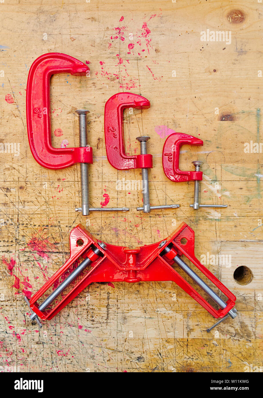 Set of three red metal C clamps and an angle clamp on red paint stained ...
