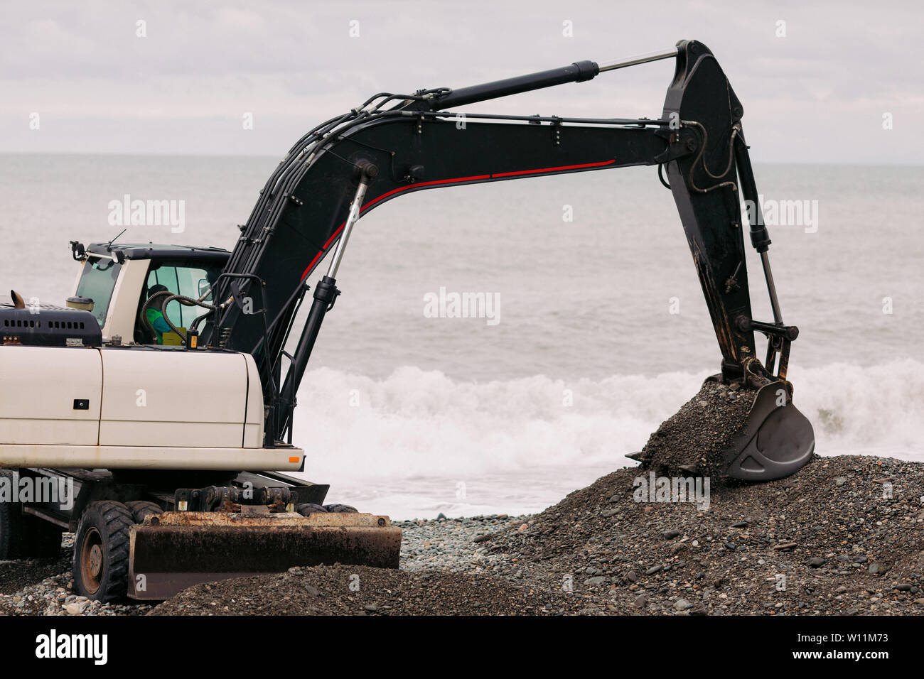 Heavy excavator working on the beach, excavator digs stones and pebbles ...