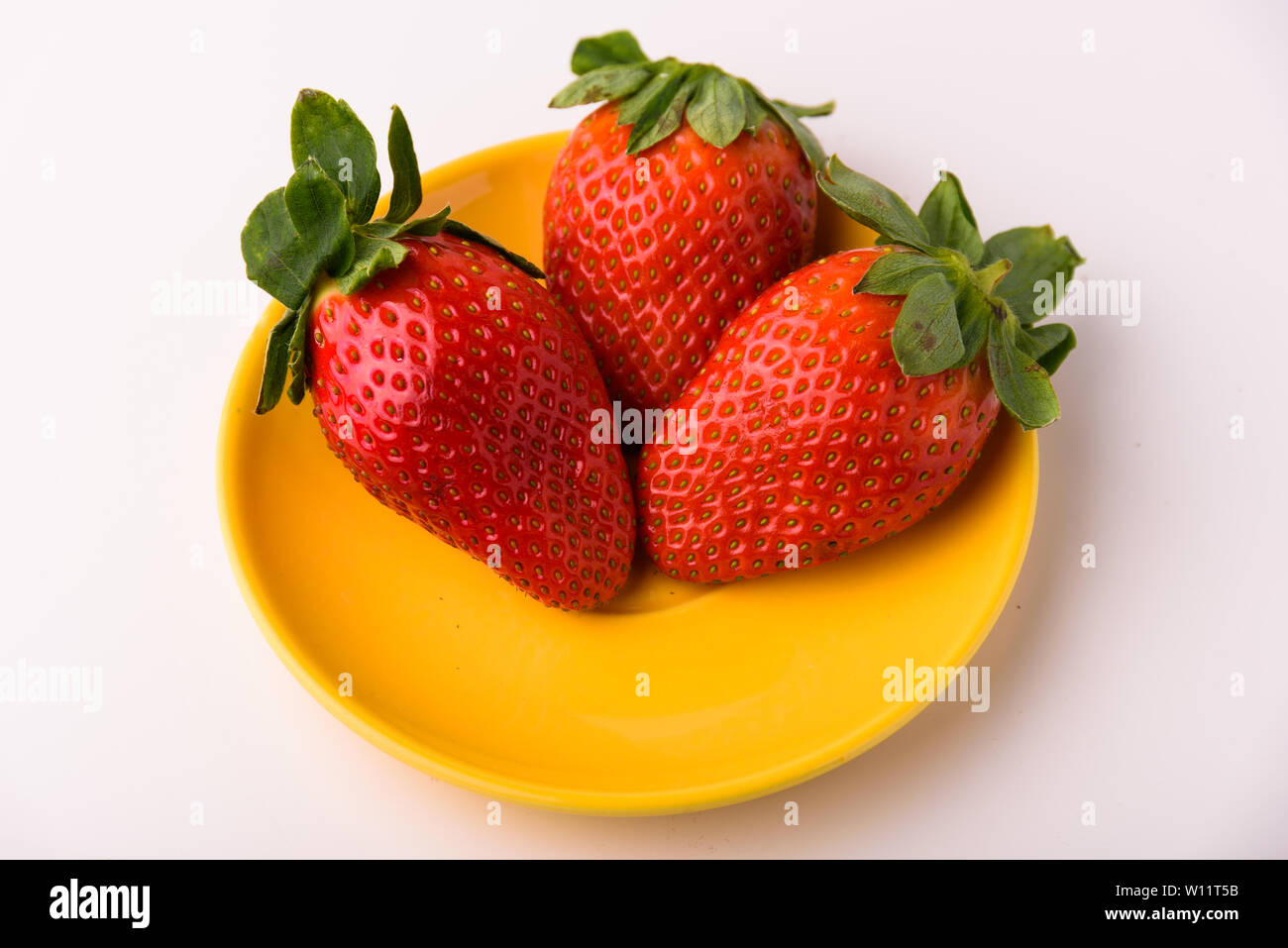 Three strawberries on a yellow plate. Isolated on a white background ...