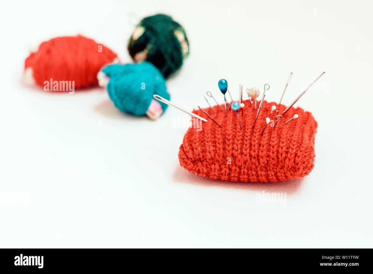Red knitted needle pad for sewing and colored thread coils on white ...