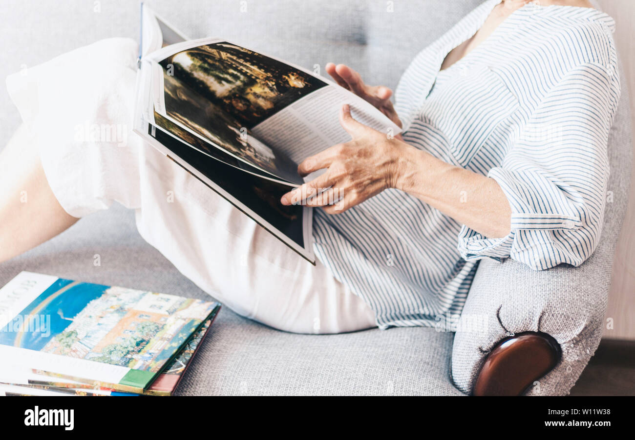 Middle-aged brunette woman on the gray sofa looking at album with ...