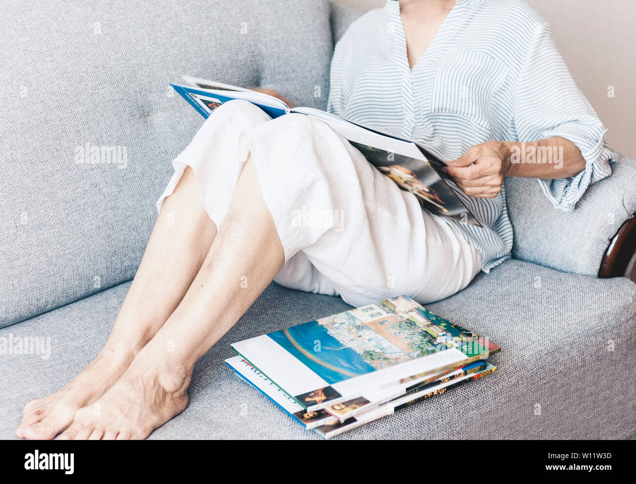 Middle-aged brunette woman on the gray sofa looking at album with ...