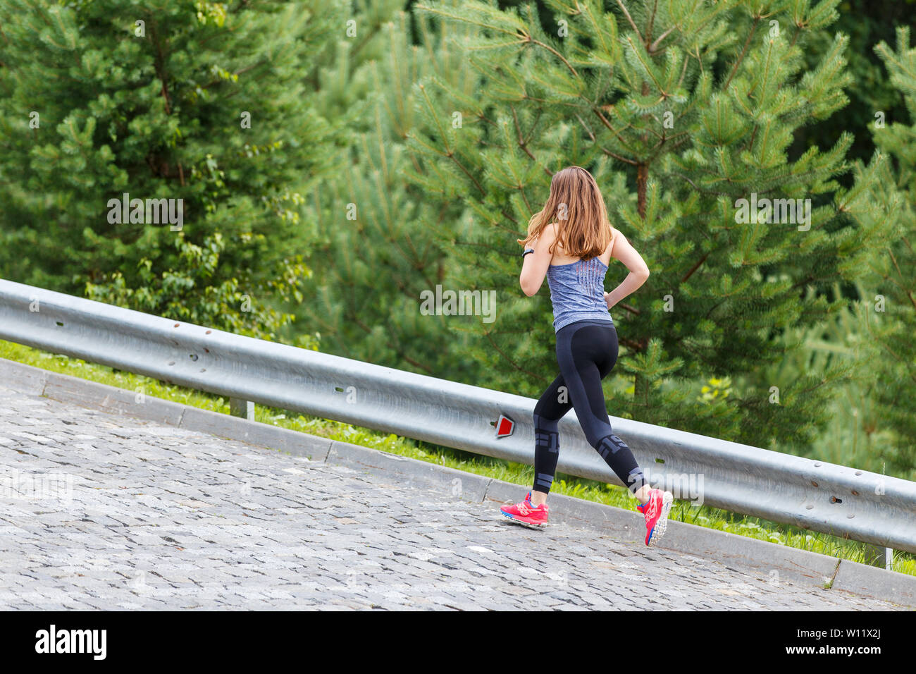 Back view of running woman on cobbled road with copy space aside. Rear ...