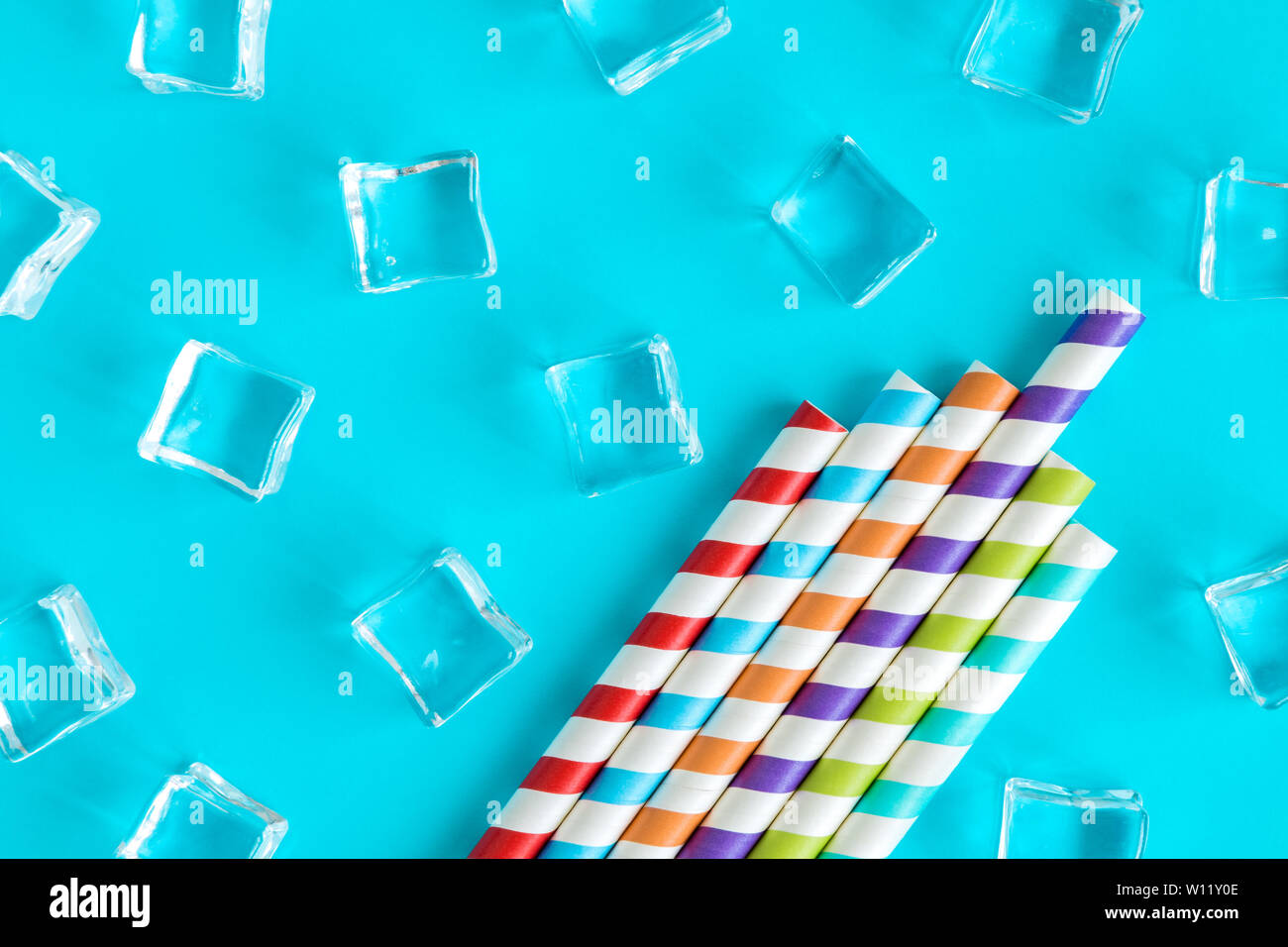 Flat lay of colorful drinking straws and ice cubes against blue ...
