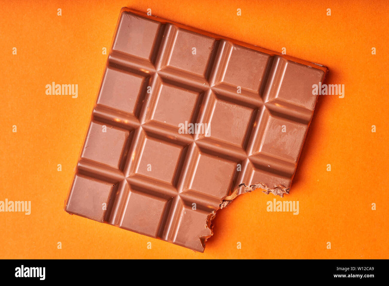Bitten bar of milk chocolate on a colored paper background Stock Photo ...