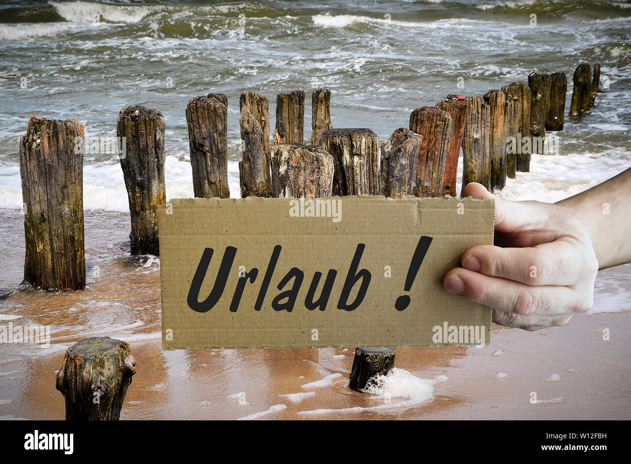 A hand holding a sign that says "Holiday" on the Baltic Sea beach Stock ...