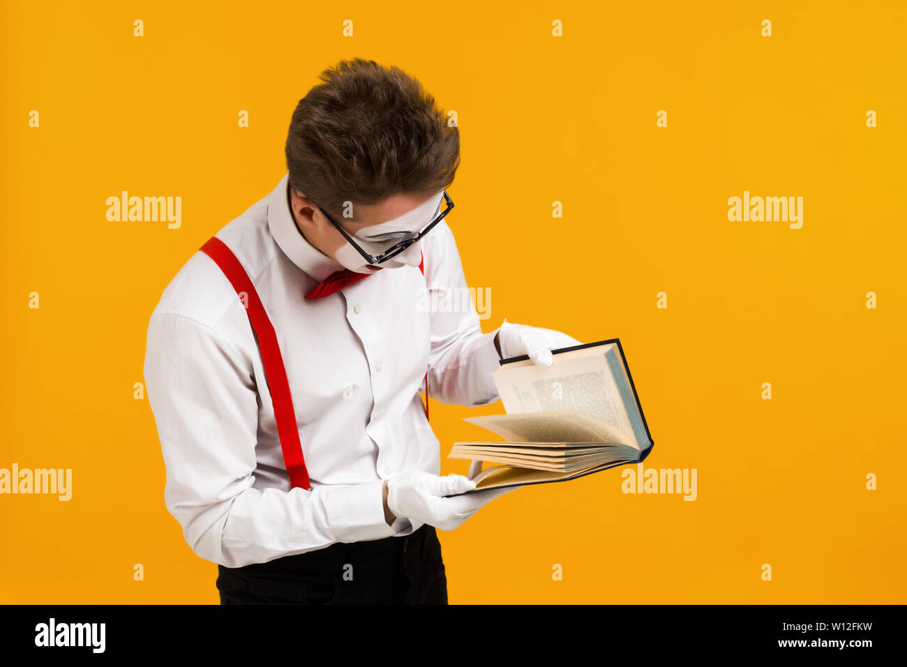 portrait of mime man artist reading book isolated on yellow background ...