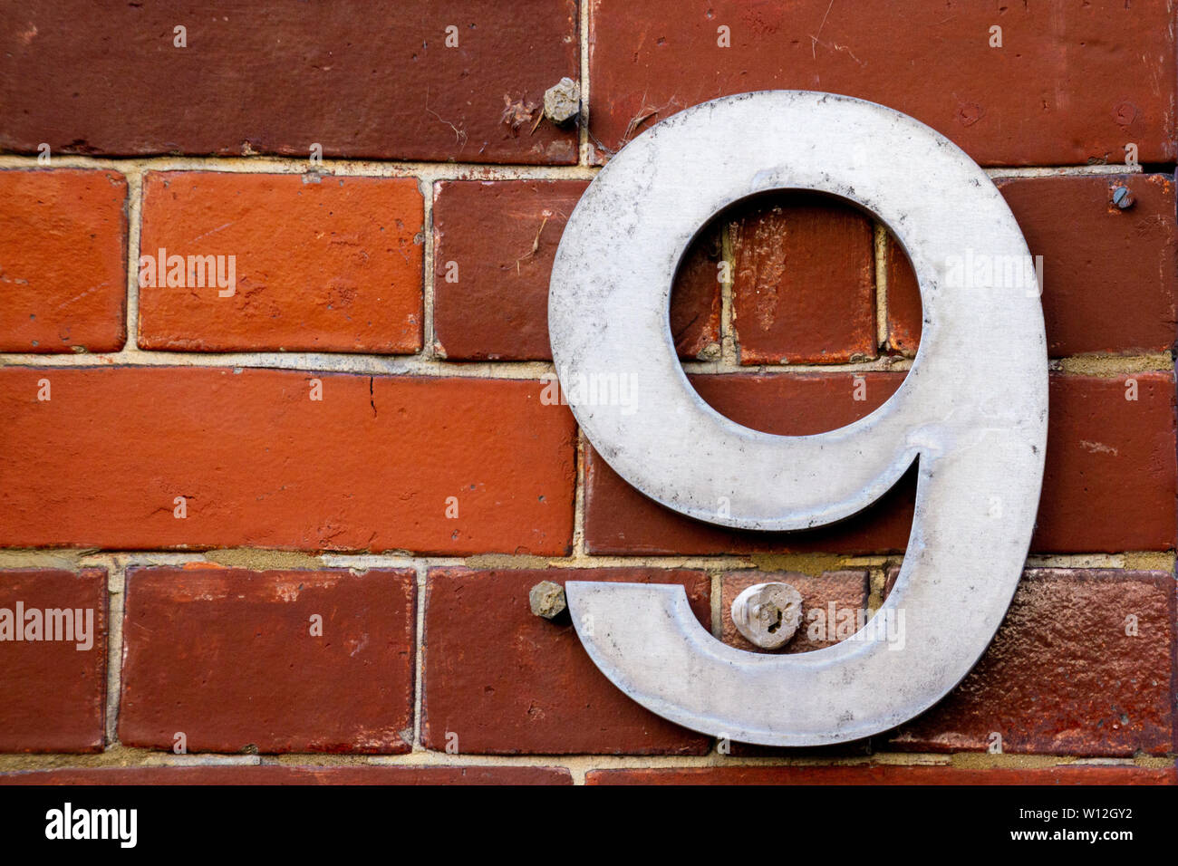 House number 9 with the nine in large brushed metal on a red brick wall ...