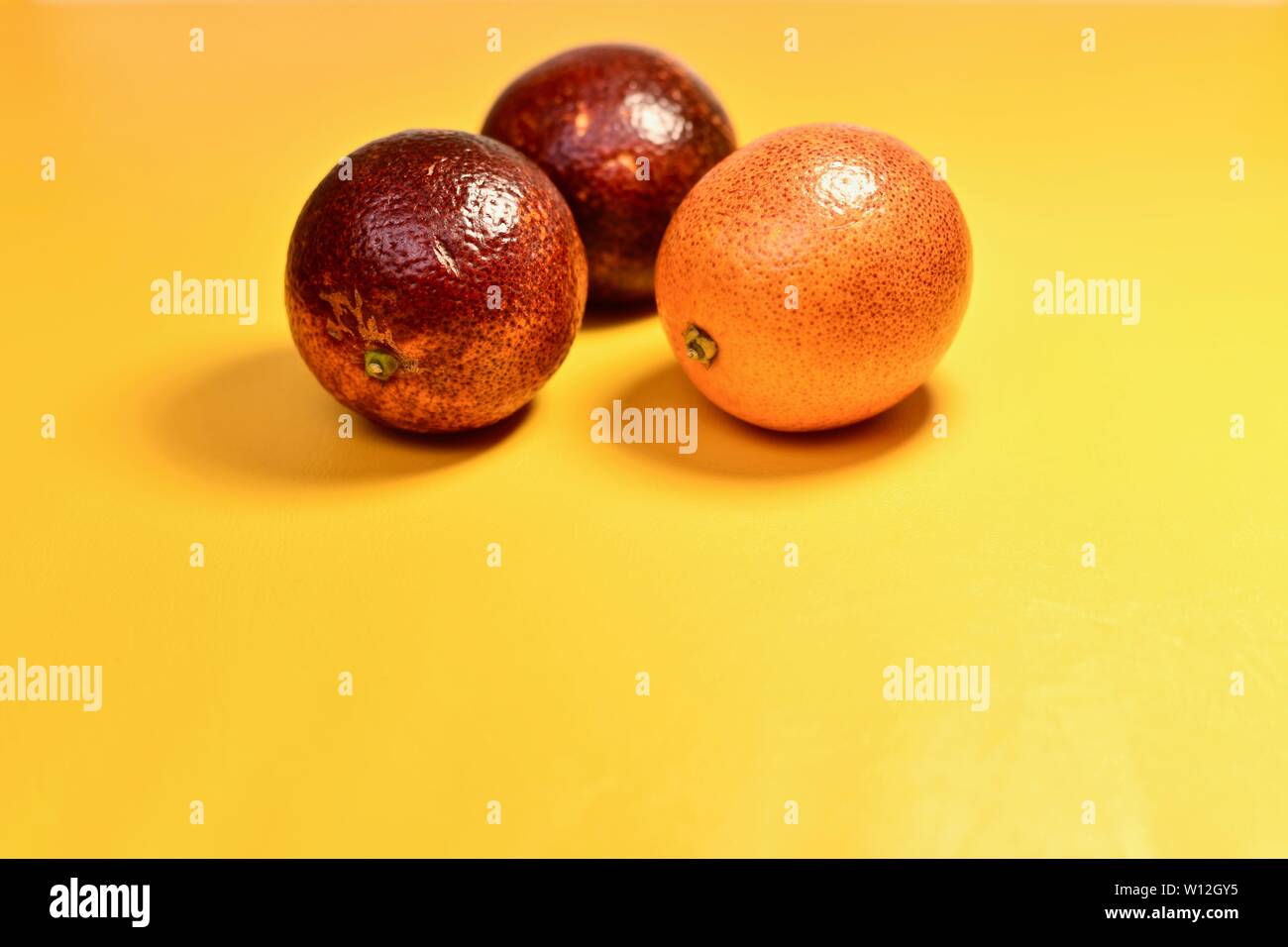 3 red oranges in the center from above on a yellow substrate. Located ...