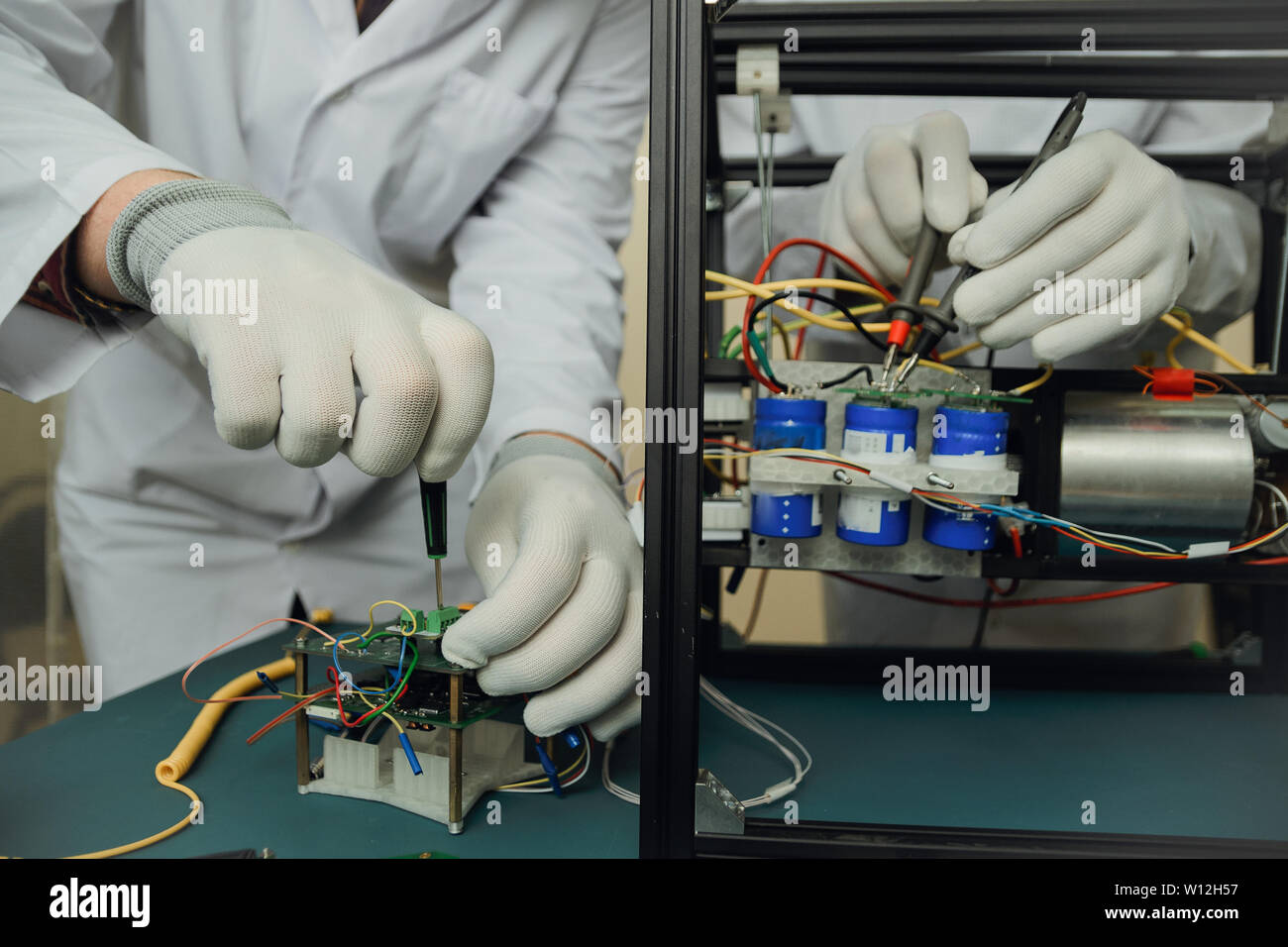 workers in gloves assemble an electrical circuit and measure the ...