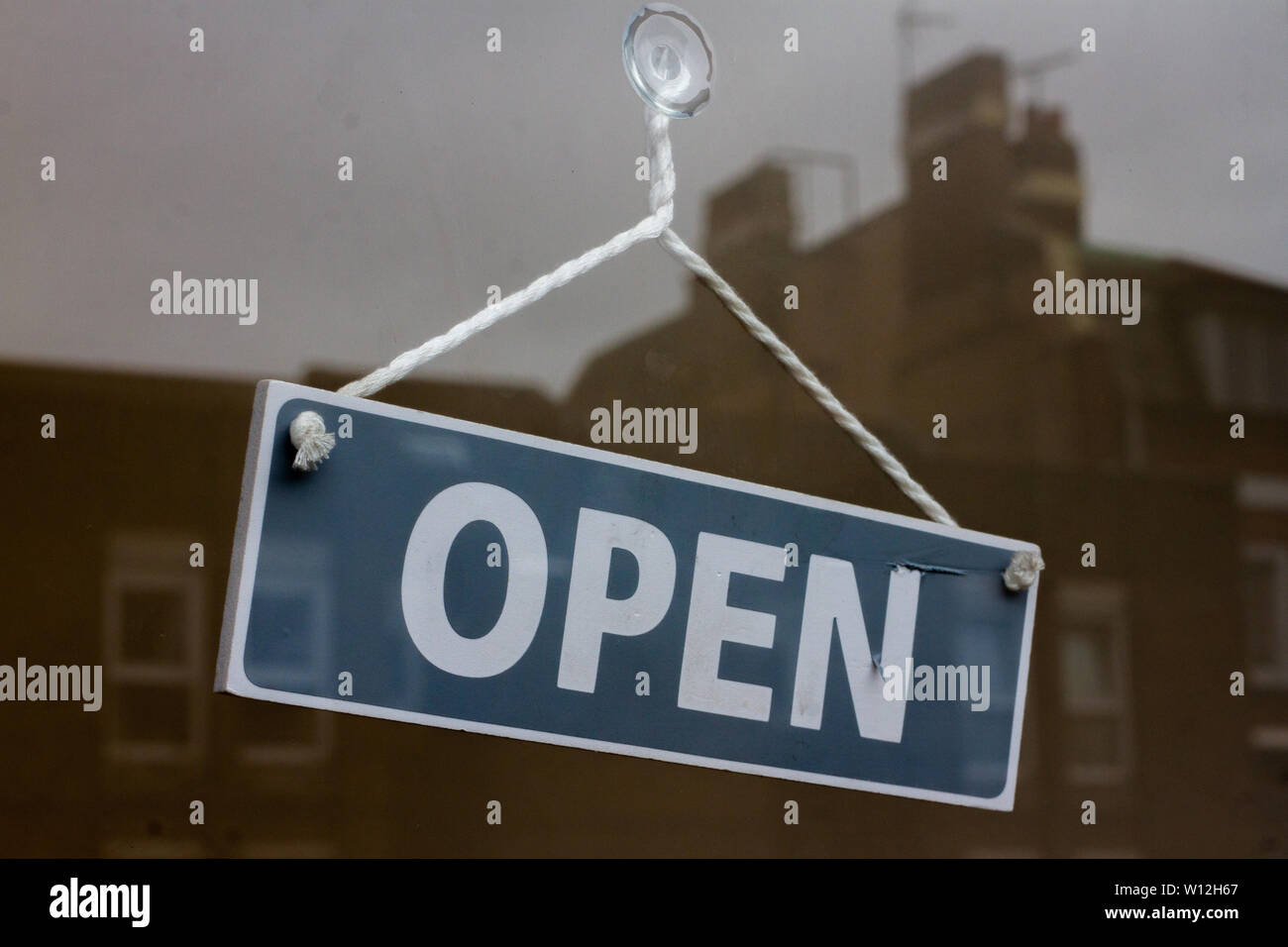 Open sign hanging crookedly behind a store window with houses reflected ...