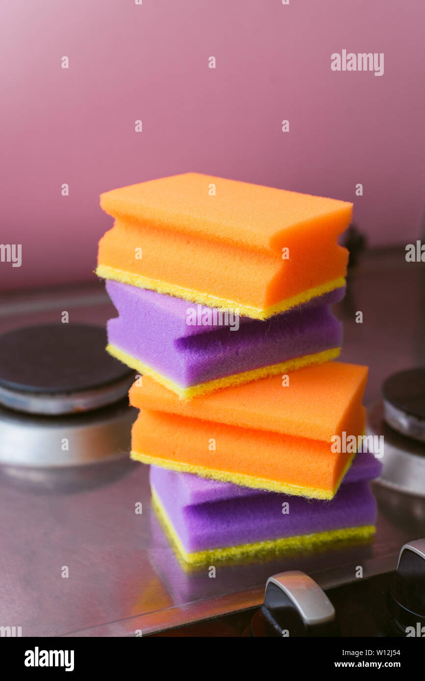 A stack of purple and orange sponges for washing on the stove. The ...
