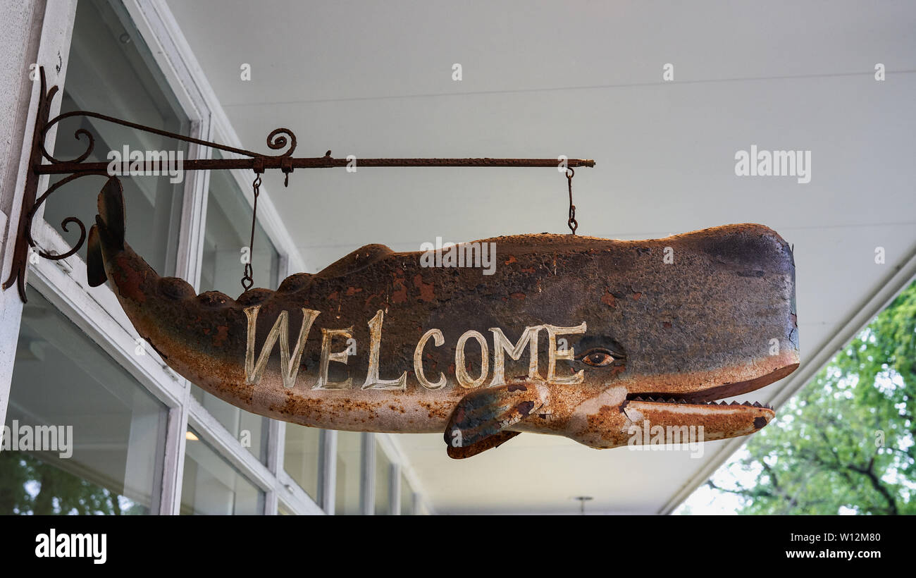 weathered and rusted whale welcome sign hanging from a bracket under a ...