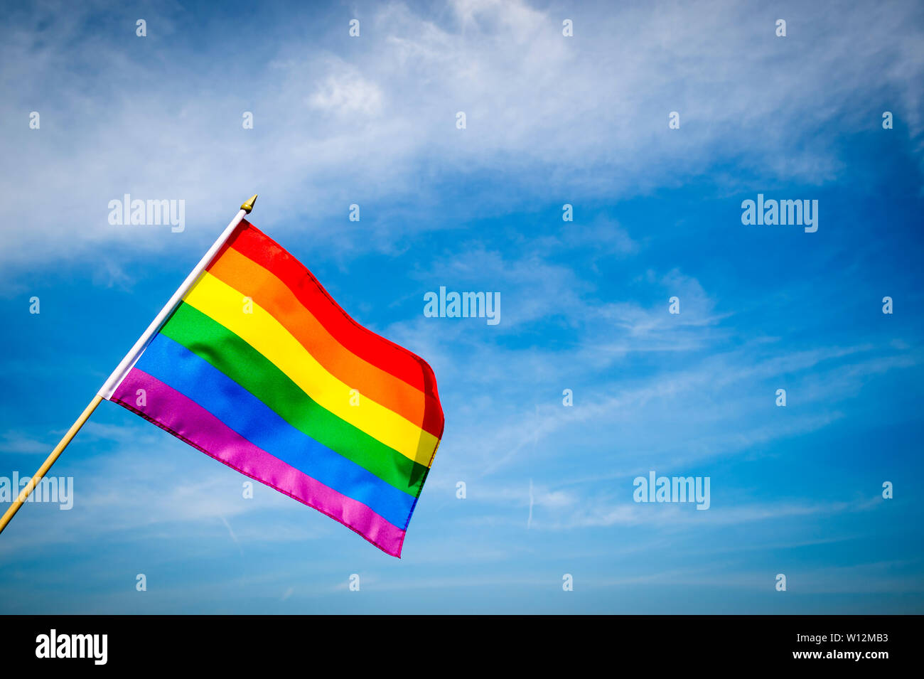 Gay LGBTQI pride rainbow flag waving in wide blue summer sky copy space ...