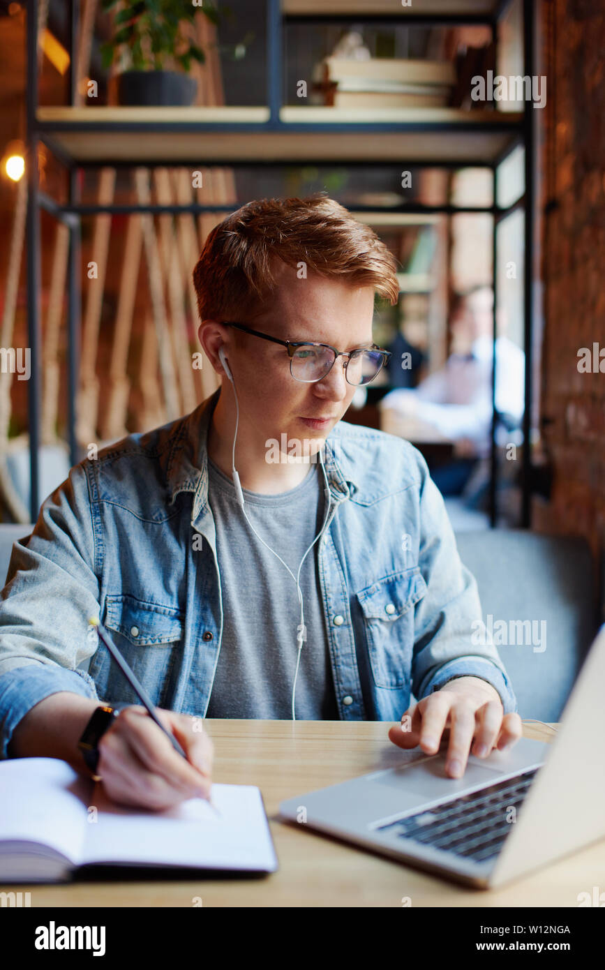 Young man wearing glasses and looking at the screen of a notebook and ...