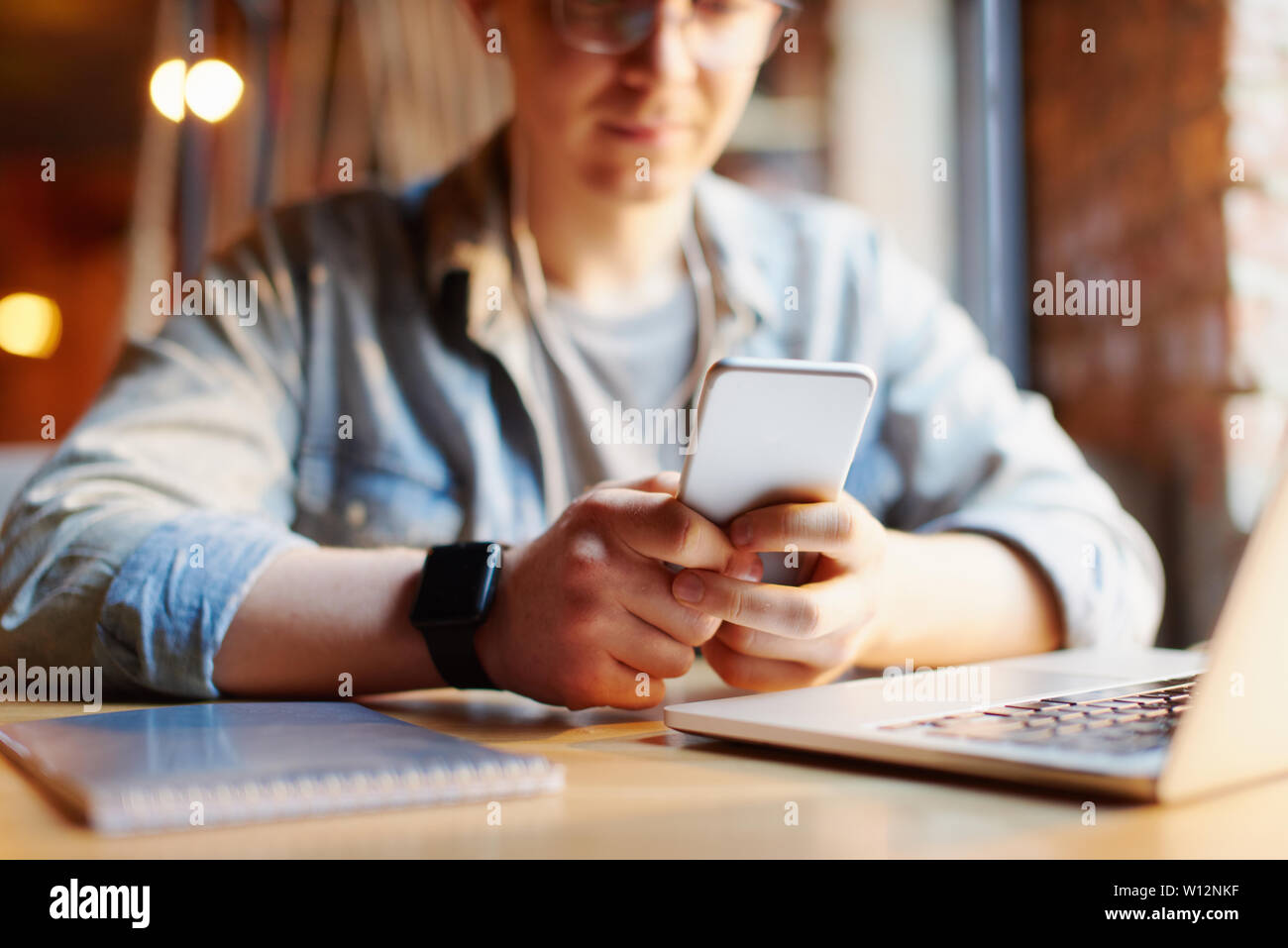 Man types on the phone screen in front of the laptop and a textbook ...