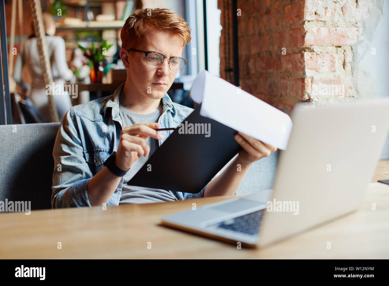 Man in glasses looking through his notes and correcting them while ...