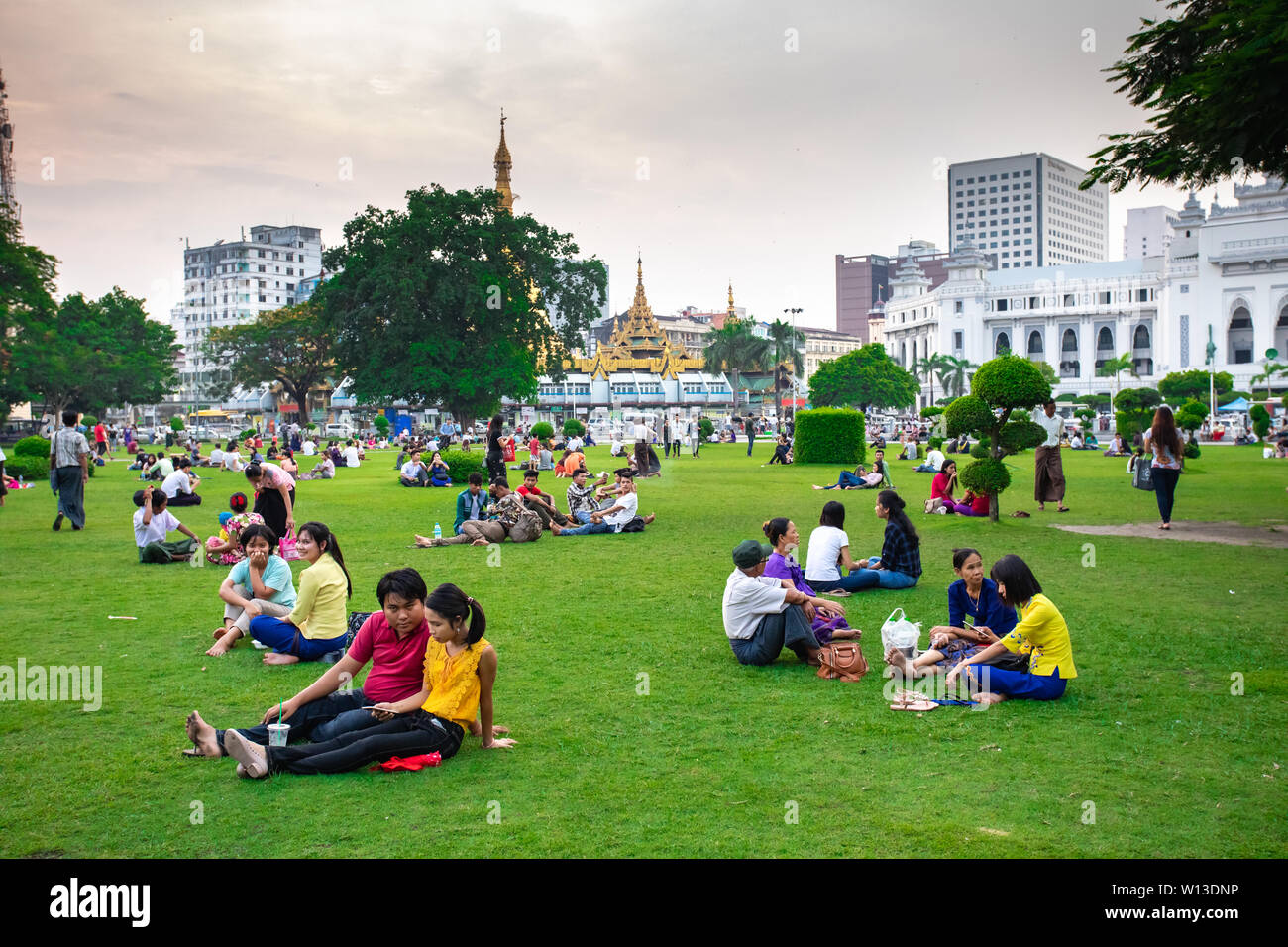 People sitting on grass in Maha Bandula park in front of Yangon City ...