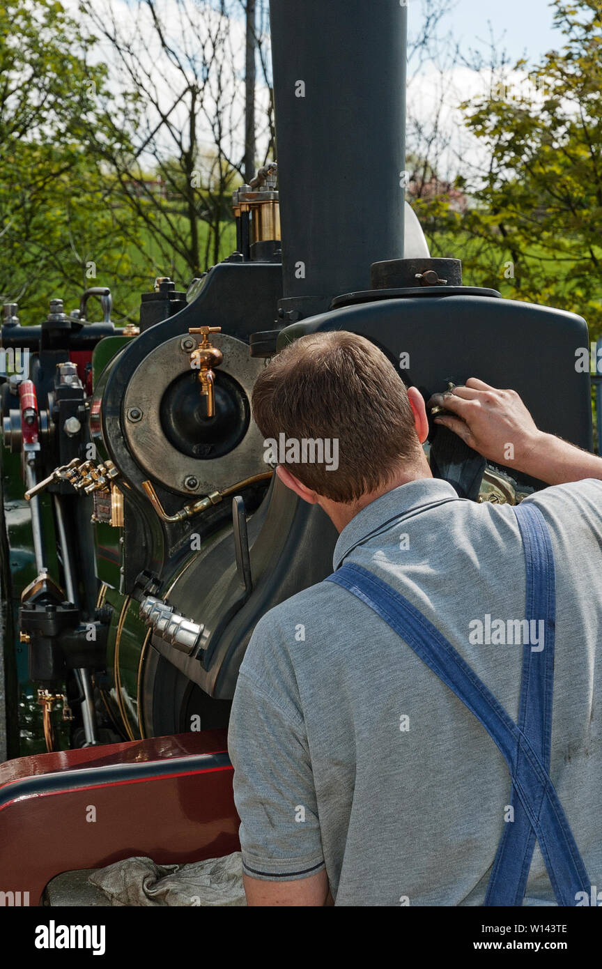 Man wearing overalls cleaning steam traction engine at classic vehicle ...