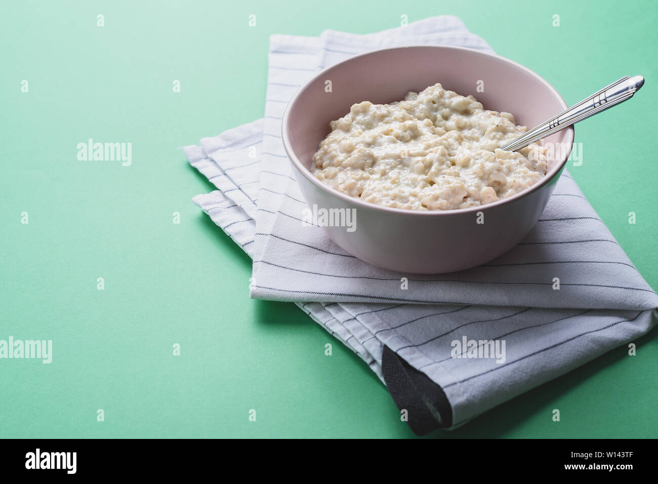 Oatmeal in a pink plate with a spoon on a white cloth, green background ...