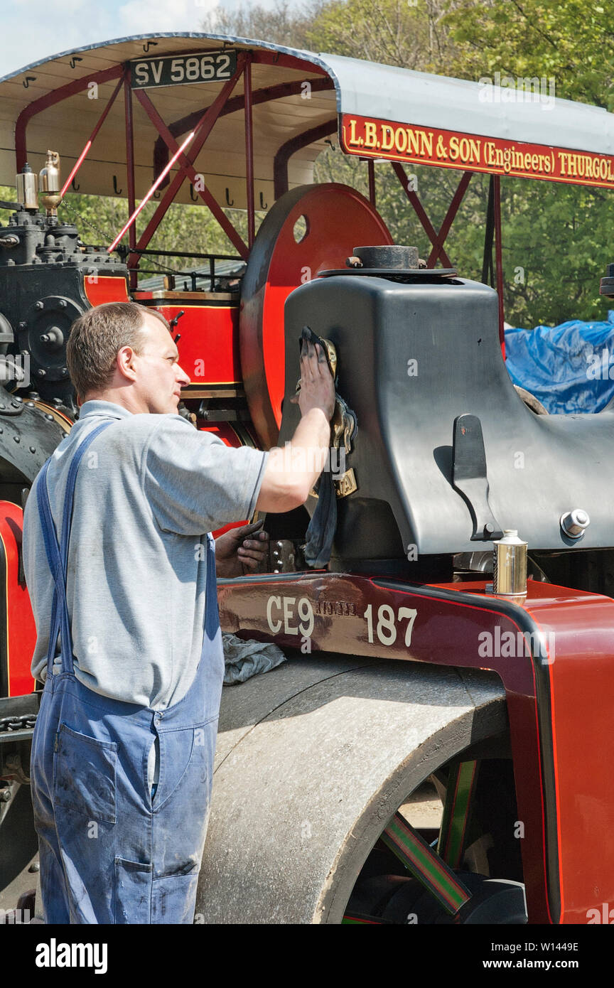 Man wearing overalls cleaning steam traction engine at classic vehicle ...
