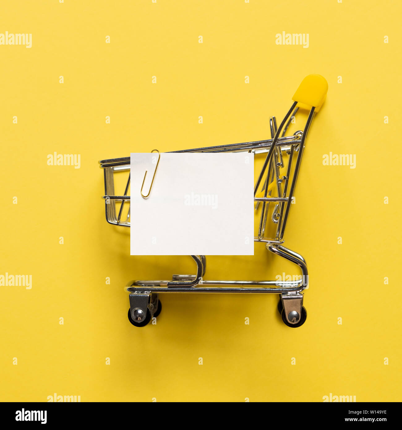 Shopping cart and white paper note list over yellow background ...