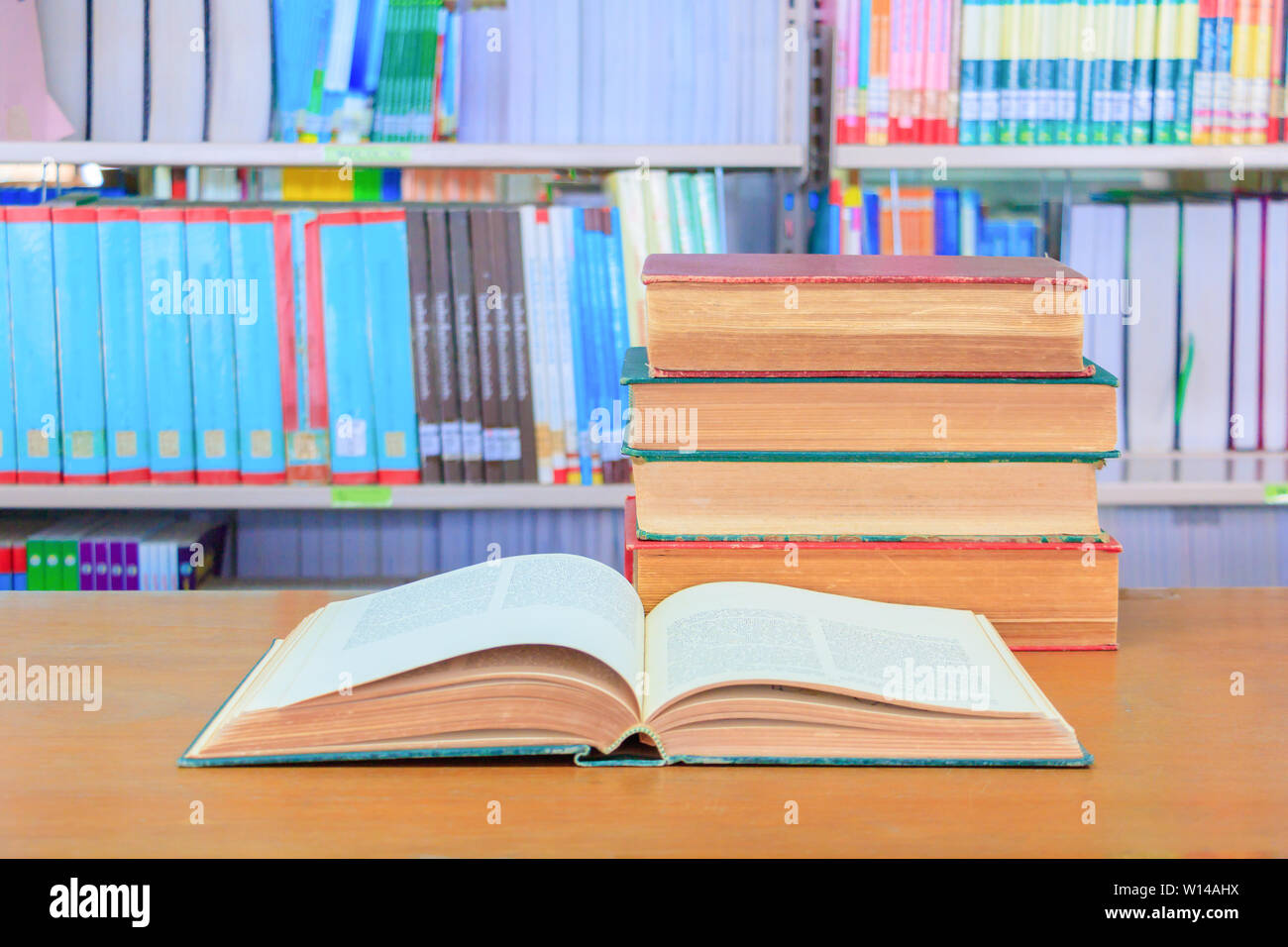 old book open in school library on wooden table. blurry bookshelves ...