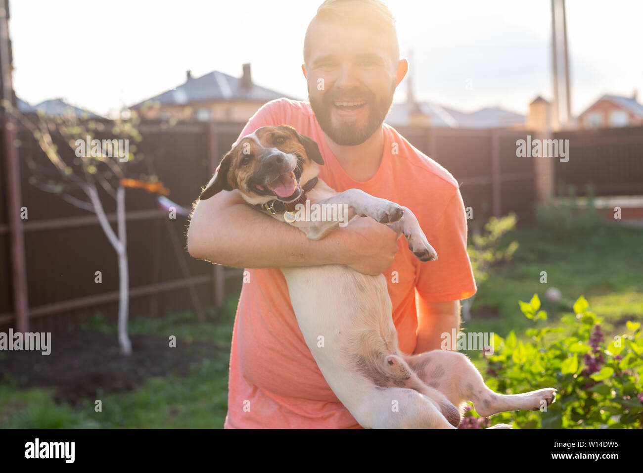 Positive young man with a beard is holding his beloved dog Jack Russell ...