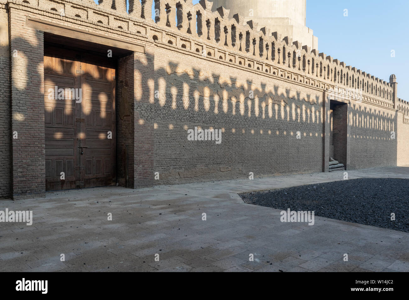 Stone bricks old decorated fence with wooden doors and shadows of ...