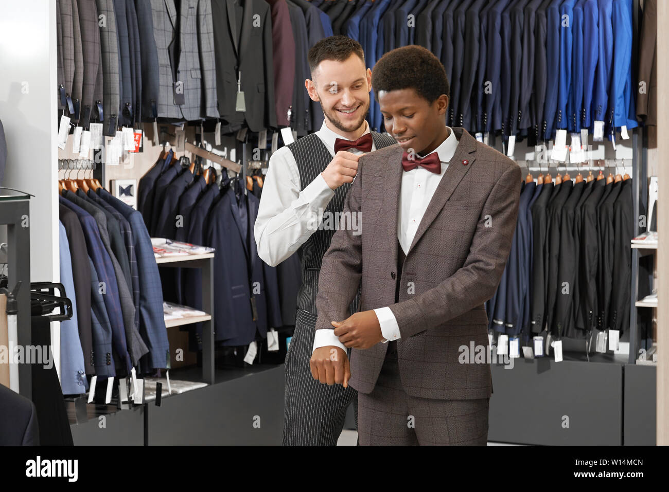 Young man choosing suit in fashionable boutique. Smiling assistants of ...