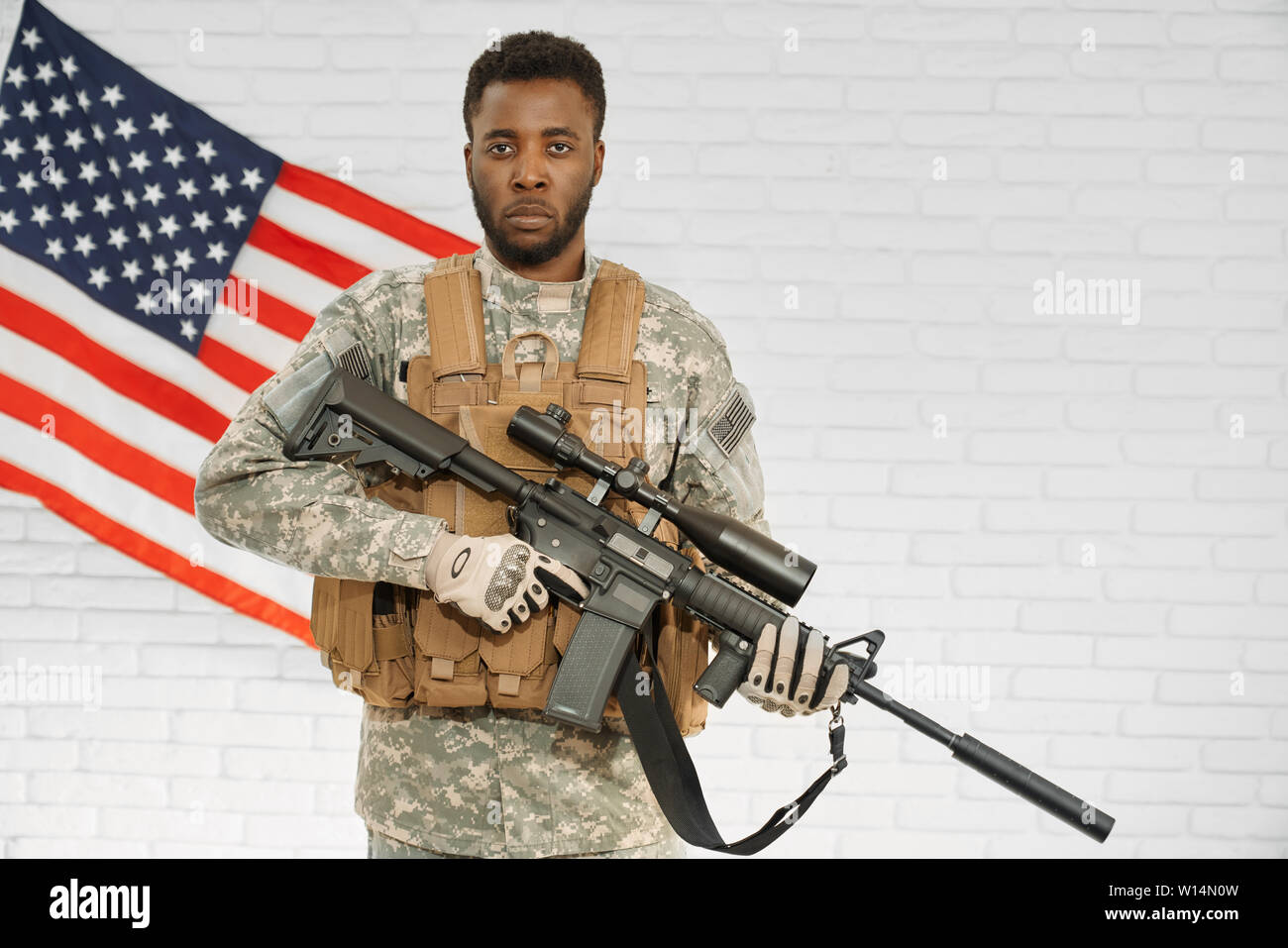 Serious American soldier with modern weapon in hands looking at camera ...