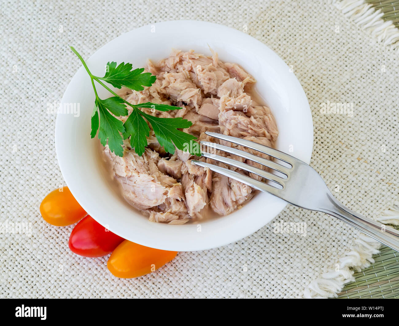 Canned tuna fillet in white porcelain bowl, fork, parsley and some ...