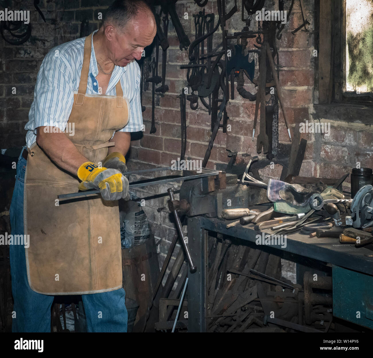 A blacksmith working in a forge, bending a heated steel bar in a vice ...