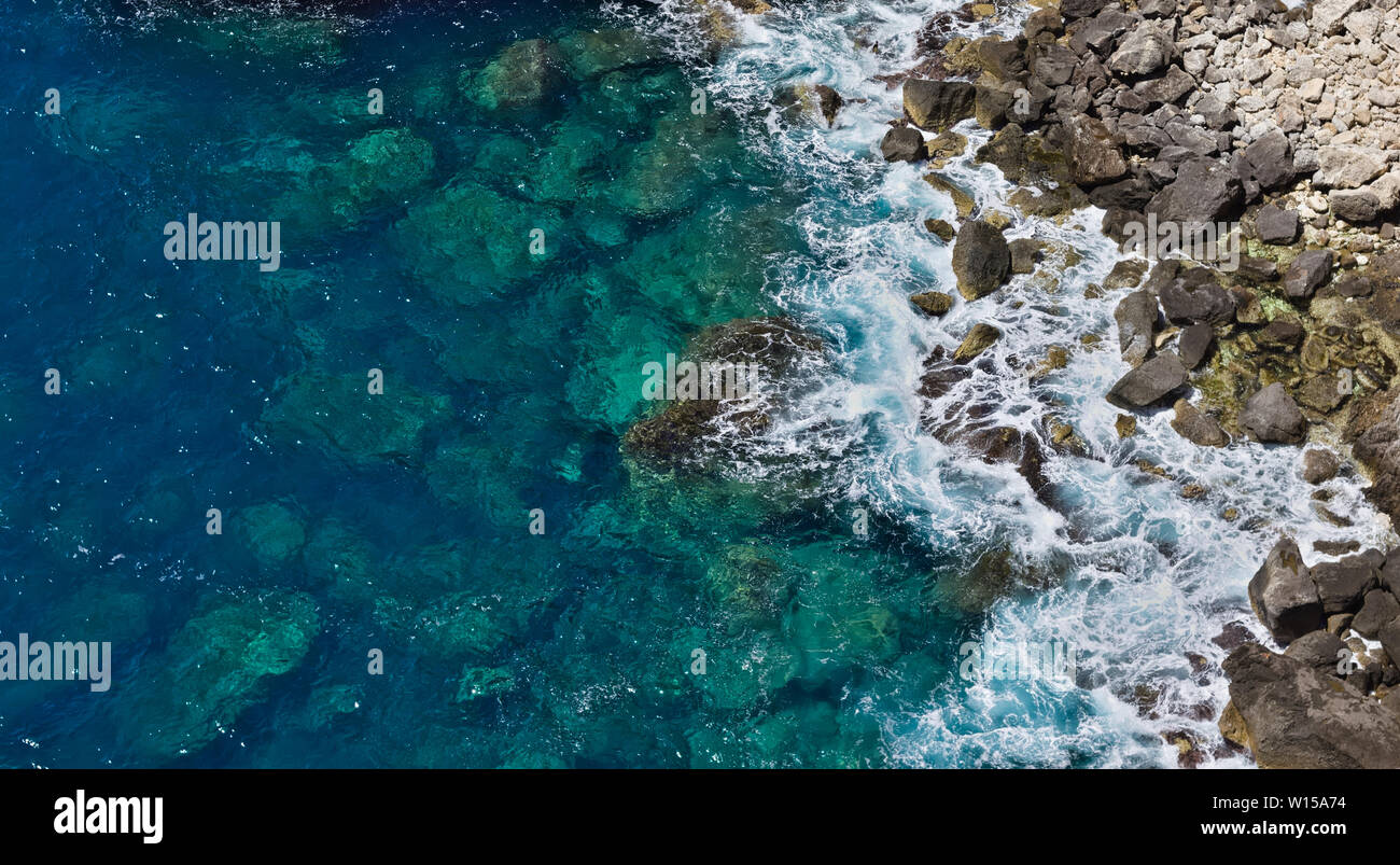 Aerial top view of crystal clear blue waves hitting rocky beach ...