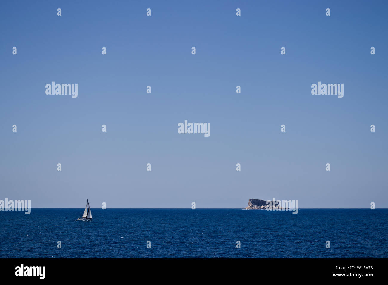 Distant Ship sailing across dark blue ocean towards small rocky island ...