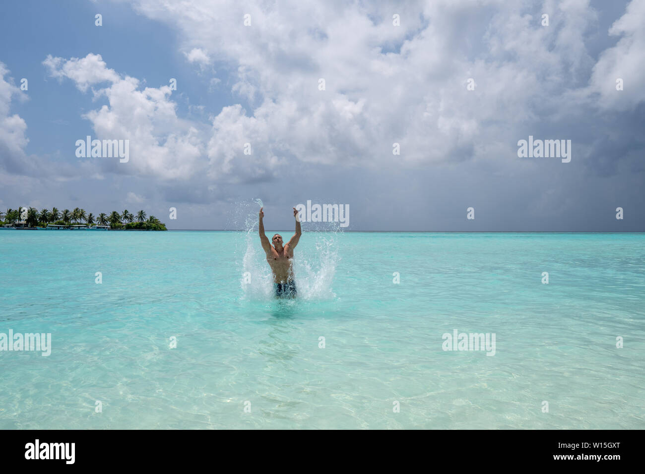 Strong young guy creates a spray of water when he jumps out of the ...