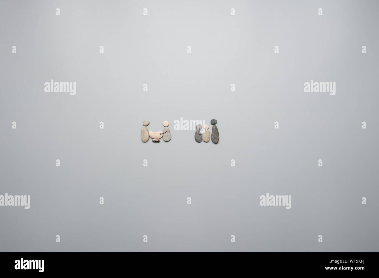 Two family units made of pebbles. Over grey background, with copy space ...